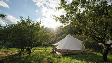 Uma tenda branca montada numa área gramada com árvores, rodeada por uma paisagem natural.