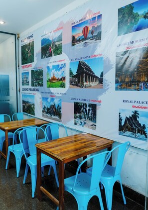 Restaurante com cadeiras azuis e mesas de madeira, decorado com cartazes de diversos pontos turísticos.