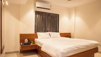 Quarto de hotel moderno com cama de madeira, mesinhas de cabeceira com chaleira e uma janela grande com cortinas.