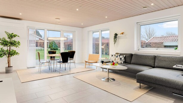 Uma sala de estar espaçosa com um sofá cinzento, uma mesa de jantar com cadeiras e uma janela grande que oferece vista para o exterior.