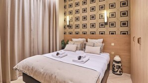 Quarto de hotel com uma cama grande, cabeceira com padrão geométrico, mesa de cabeceira com um vaso e cortina na janela.