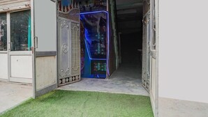 Entrada de um edifício com porta protegida por grades, pequena área gramada na frente e portão de metal decorativo com desenhos detalhados.