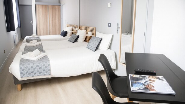 Quarto de hotel com duas camas, uma mesa e uma cadeira.