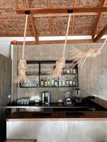 Área de bar com bancada de concreto, máquina de café, liquidificador e prateleira com garrafas.