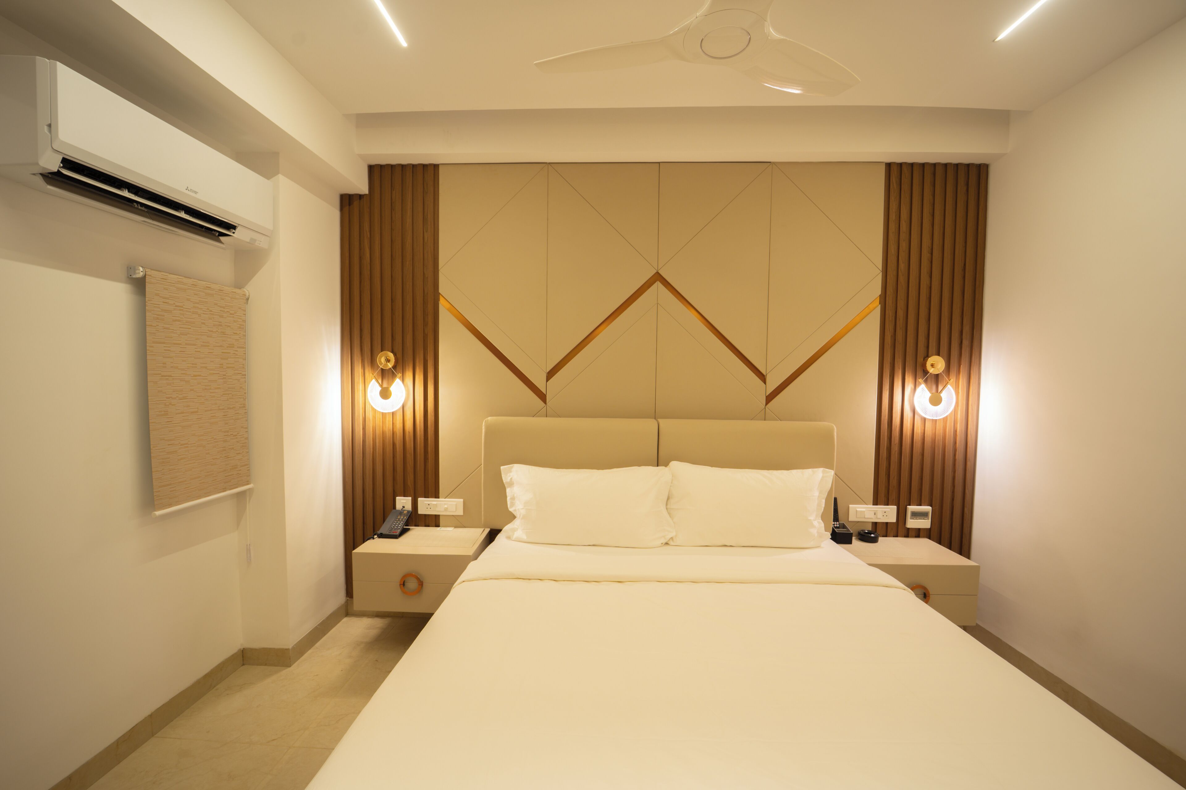 Quarto de hotel moderno com uma cama grande, cabeceira de madeira e duas mesas de cabeceira com luminárias.