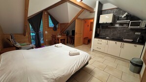 Quarto com uma cama grande, teto de madeira, uma kitchenette pequena e um espaço de jantar com mesa e cadeiras.