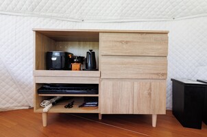 Um armário compacto de madeira com cafeteira embutida, chaleira e uma pequena prateleira com dispositivos eletrônicos.