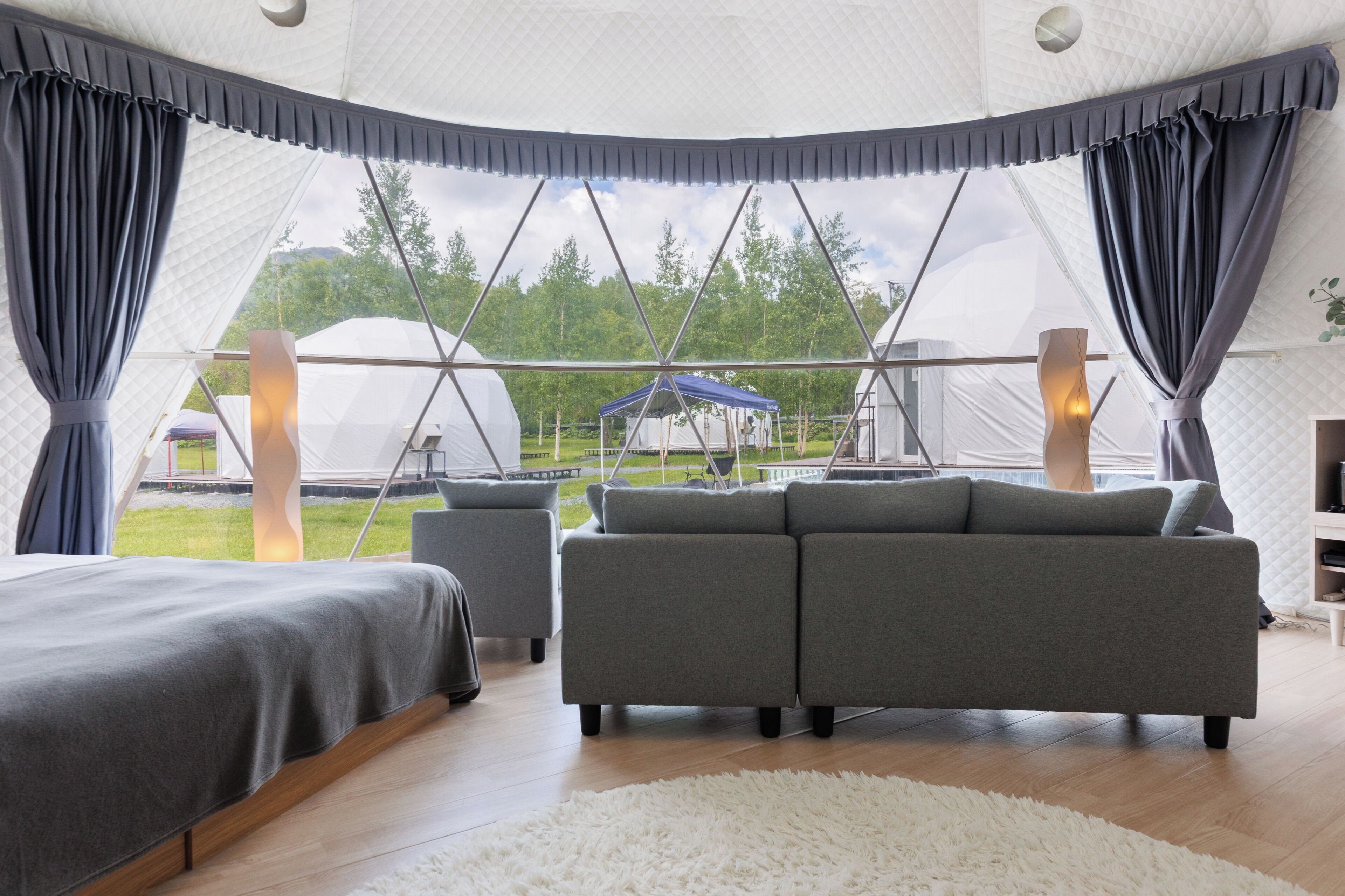 Acomodação em tenda moderna com sofá, uma cama, um tapete branco e fofo, e vista para o exterior.