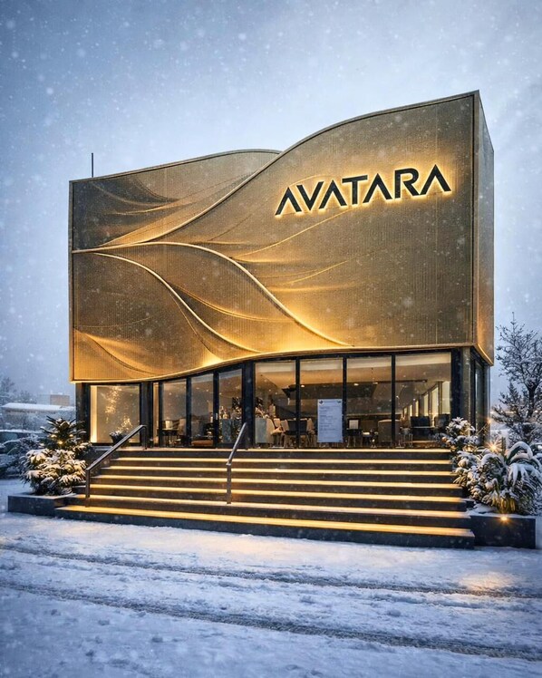 Um edifício moderno com o nome "AVATAR" em destaque. Apresenta uma fachada curva com grandes janelas e uma escadaria que leva à entrada.