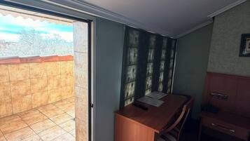 Um pequeno espaço de escritório com uma mesa, cadeira e vista através de uma porta de vidro deslizante.