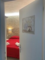 Quarto com parede de pedra, cama com colcha vermelha e obra de arte na parede com conchas.