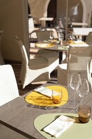 Uma sala de jantar com cadeiras de vime, uma mesa posta com jogos americanos amarelos, copos de vinho e um menu.