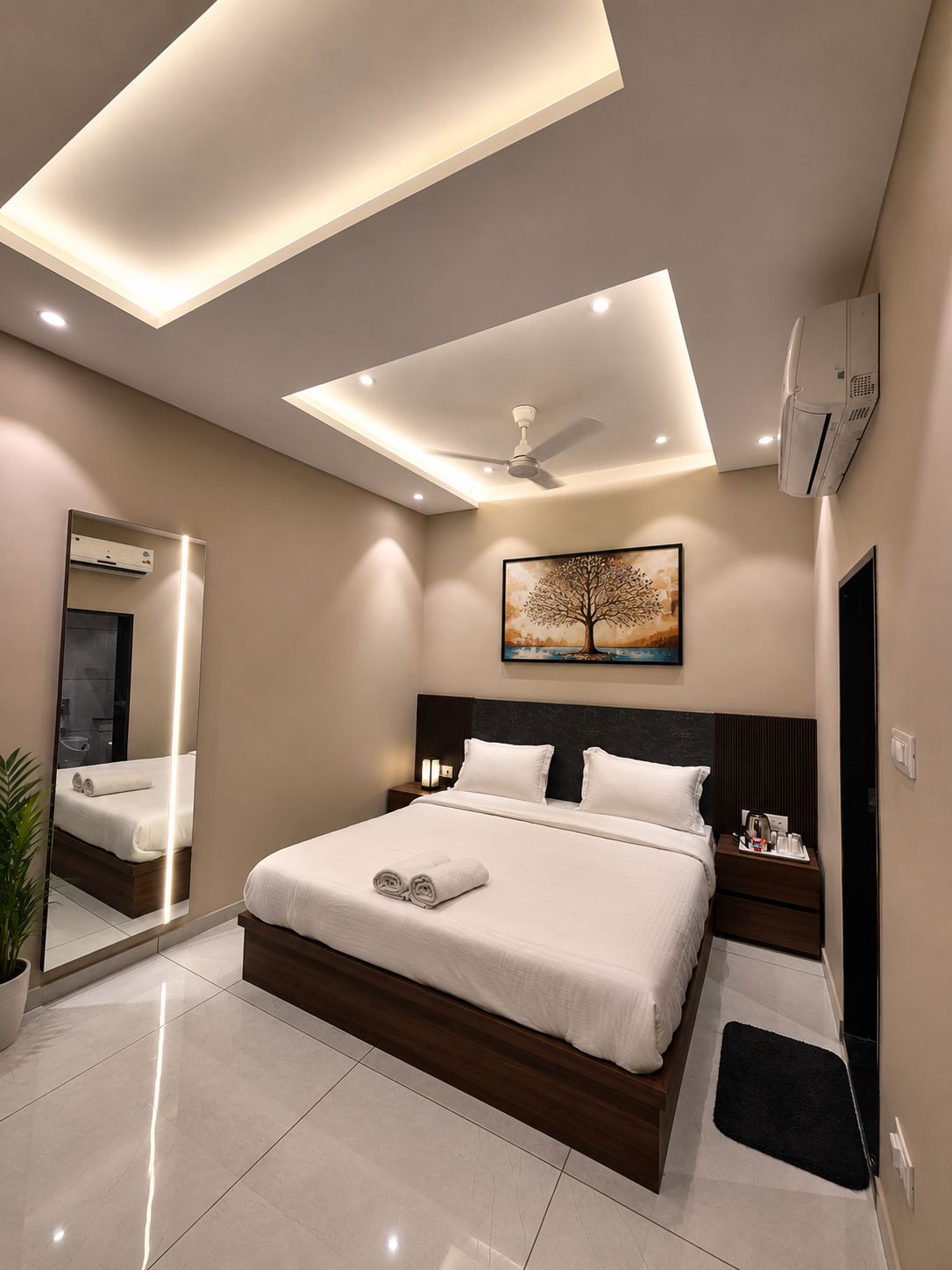 Quarto de hotel moderno com uma cama grande, ventoinha no teto, iluminação embutida, um quadro e um espelho.