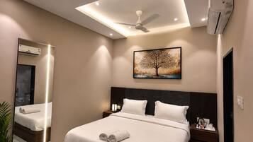 Quarto de hotel moderno com uma cama grande, ventoinha no teto, iluminação embutida, um quadro e um espelho.