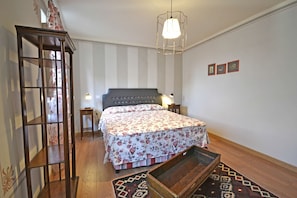 Quarto com cama, mesa de cabeceira, luminária, armário de madeira e tapete estampado.