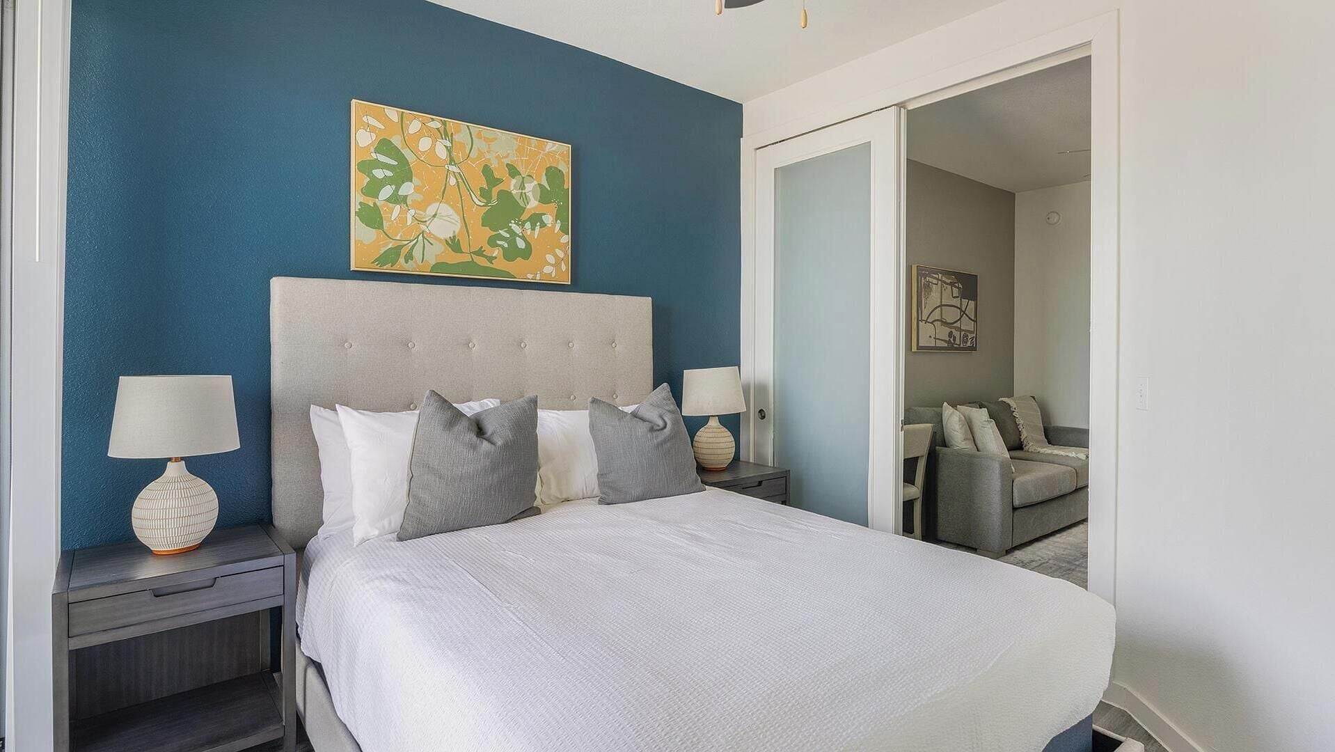 Quarto com cama grande, duas mesas de cabeceira com abajures, cabeceira e um quadro na parede.