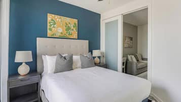 Quarto com cama grande, duas mesas de cabeceira com abajures, cabeceira e um quadro na parede.
