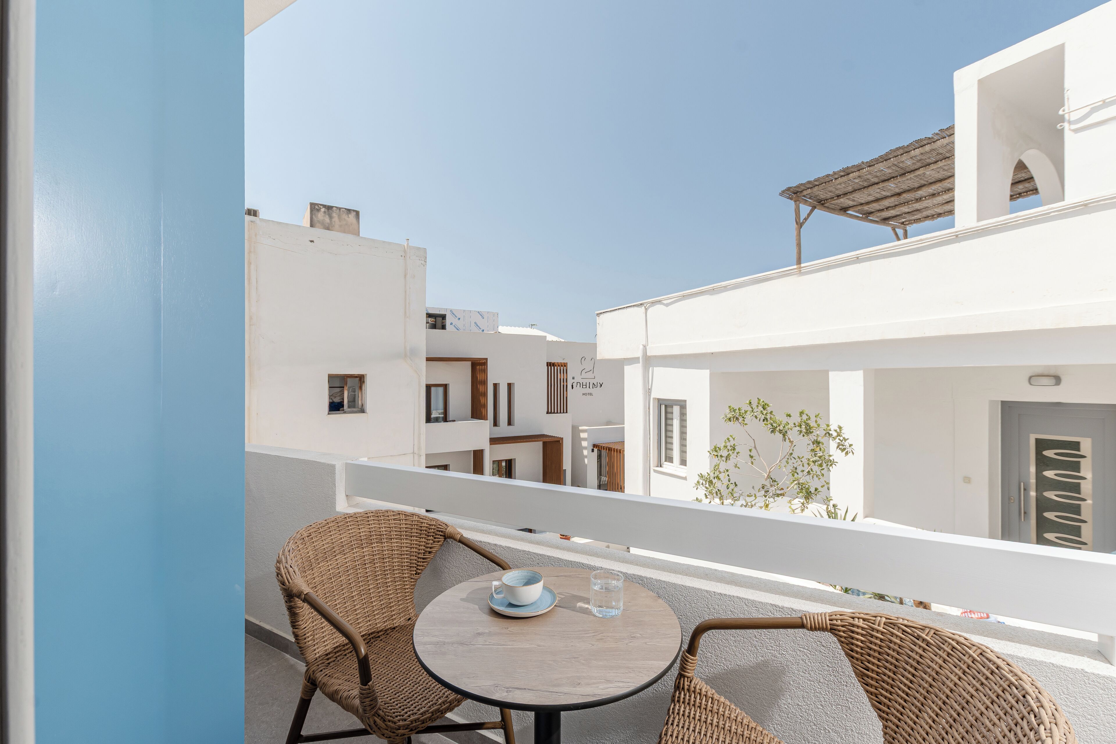 Varanda com cadeiras de vime e uma mesa, com vista para um edifício branco com varandas.