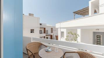 Varanda com cadeiras de vime e uma mesa, com vista para um edifício branco com varandas.