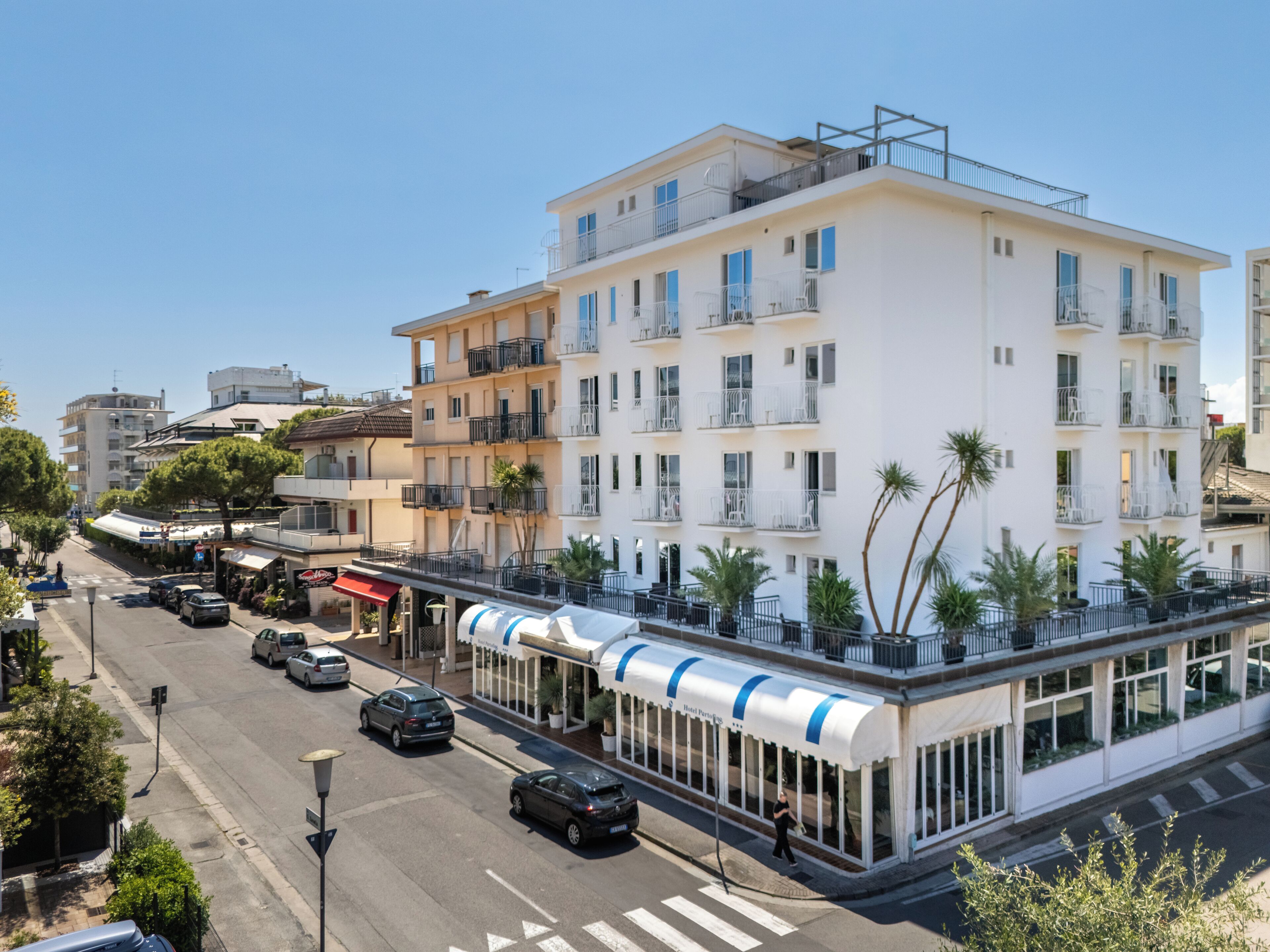 Hotel de vários andares com varandas, área de estar coberta ao ar livre e vista para a rua com carros estacionados.