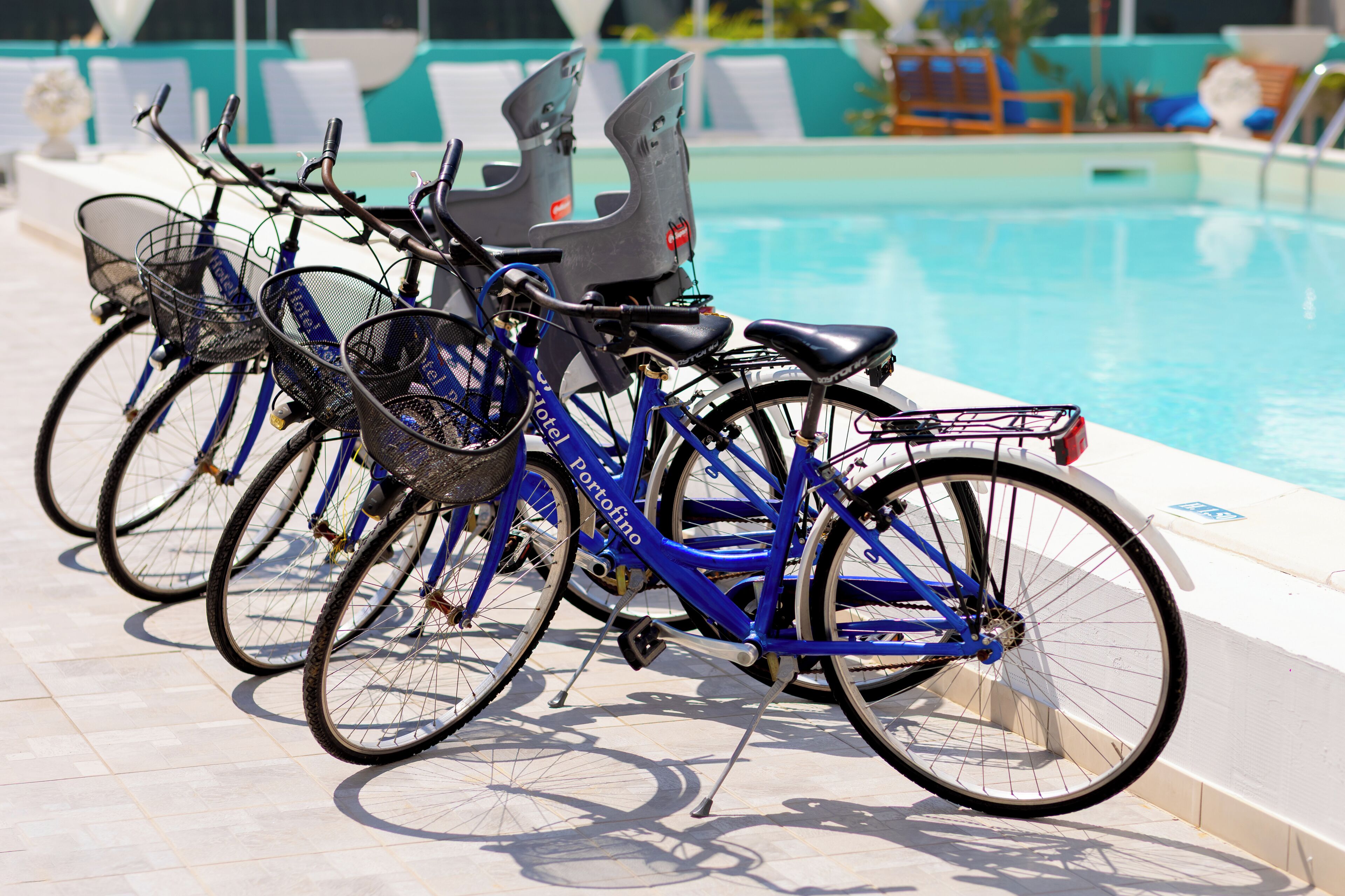 Uma fileira de bicicletas azuis com cestas estacionadas à beira da piscina.