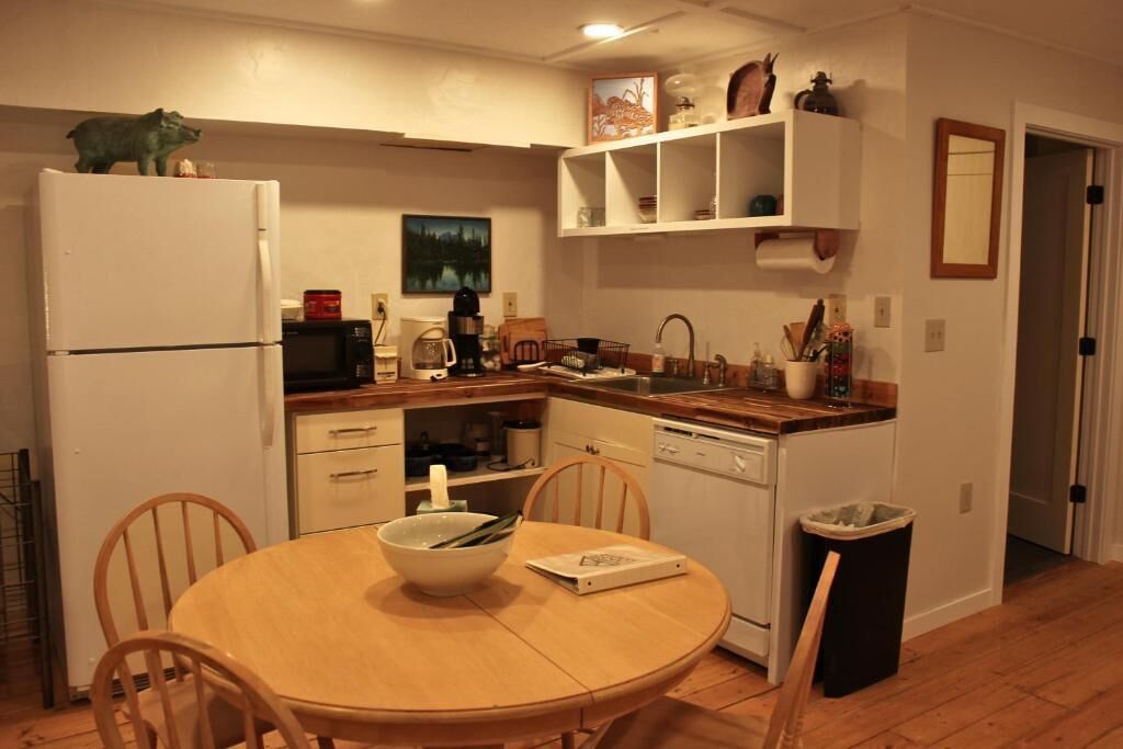 Uma cozinha compacta com geladeira, micro-ondas, pia e mesa de jantar de madeira.