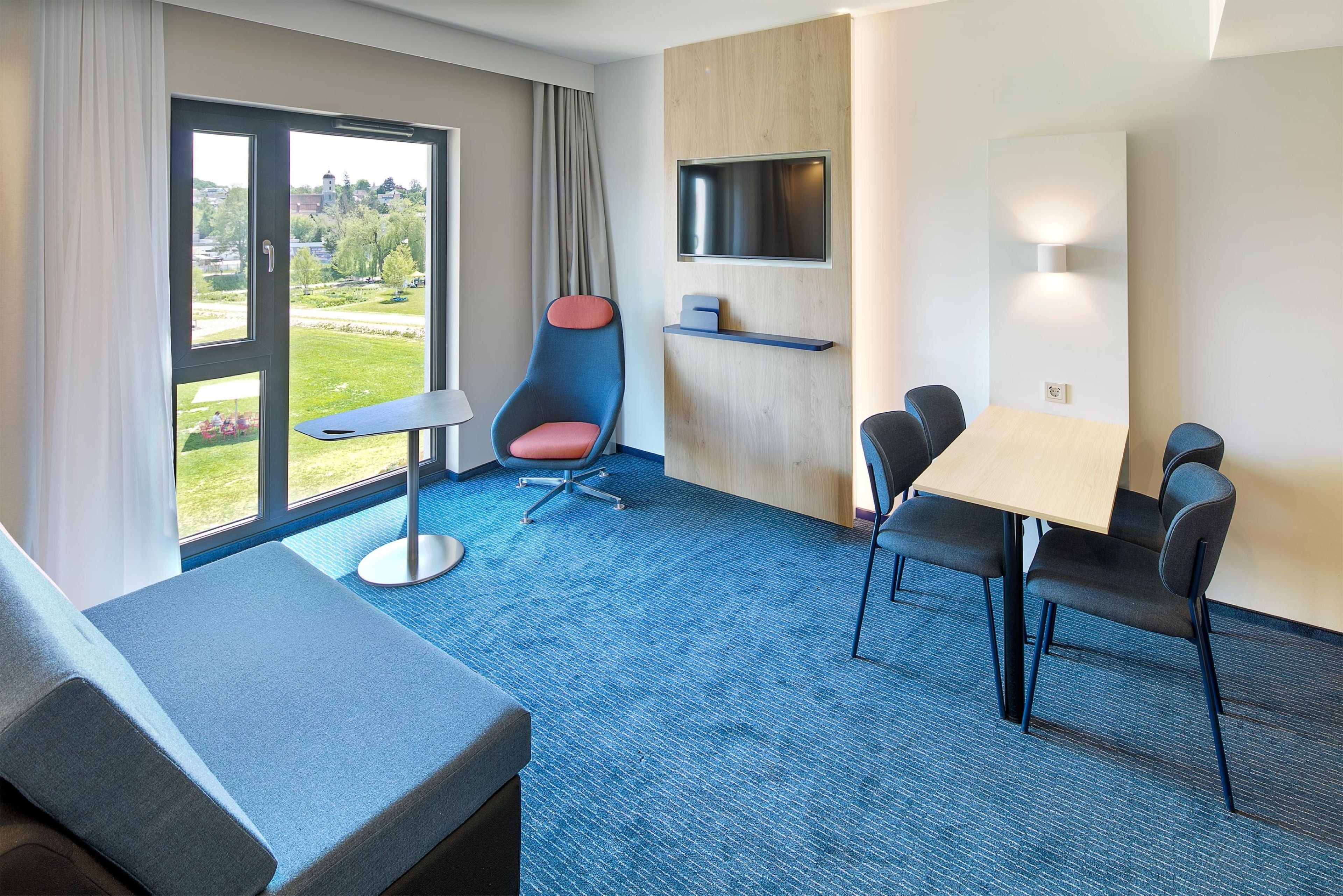 Quarto de hotel com cama, escrivaninha, poltrona, televisão e vista para o exterior.