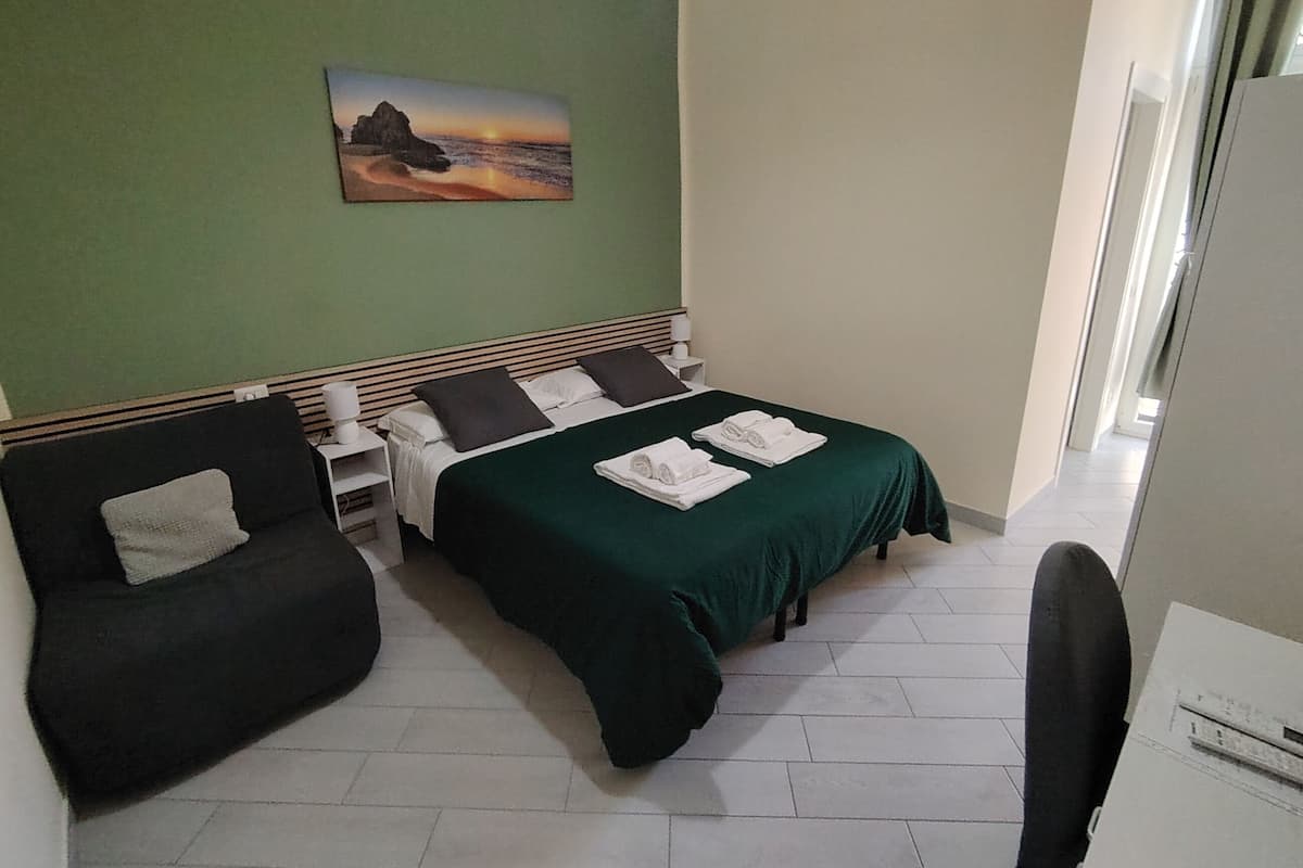 Quarto pequeno e limpo com cama, uma cadeira e uma escrivaninha.