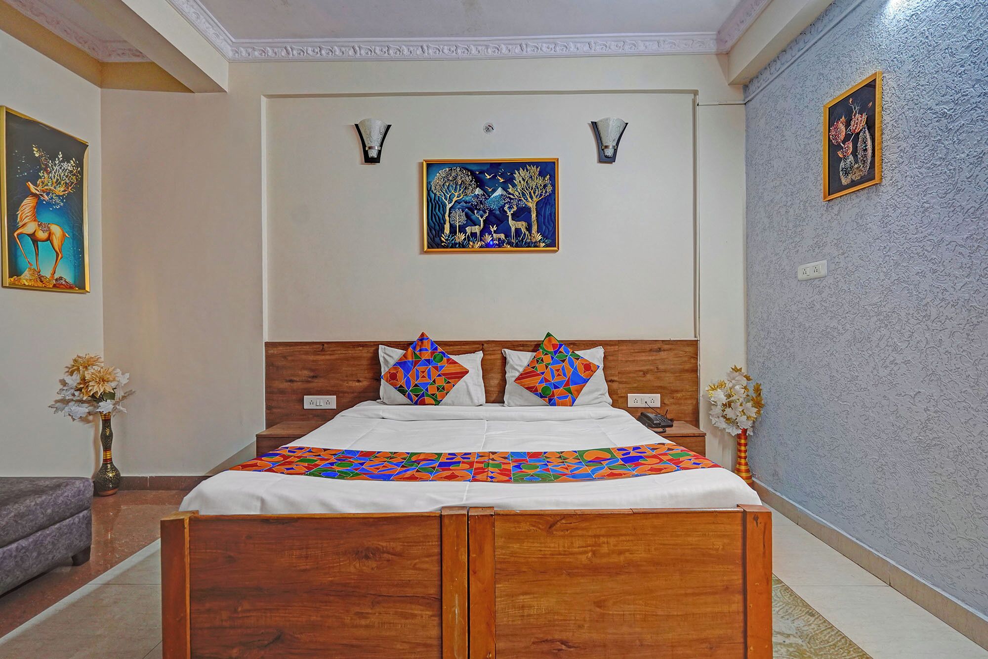 Quarto com cama de madeira, roupa de cama branca e almofadas geométricas coloridas.