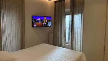 Quarto de hotel com uma cama, televisão fixada na parede e uma janela com cortinas.