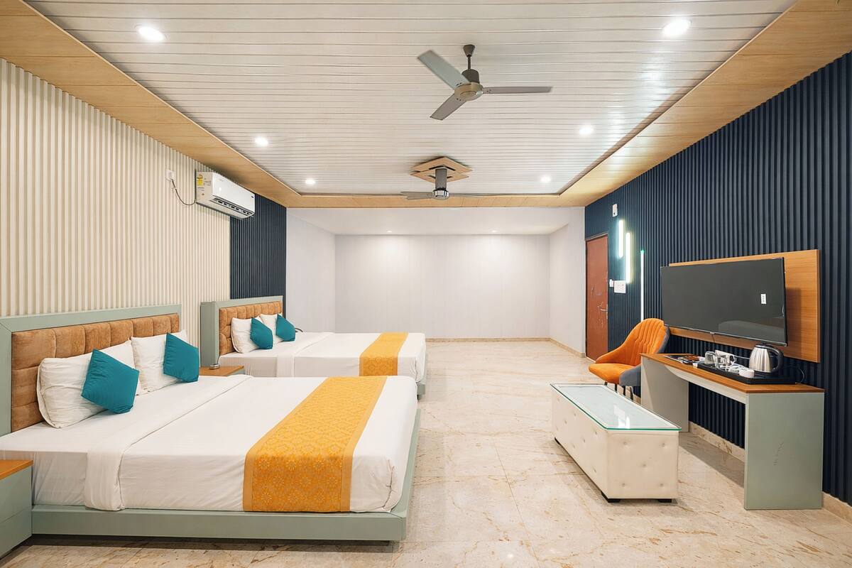 Quarto de hotel com duas camas, uma escrivaninha, uma cadeira, uma televisão e um ventilador de teto.
