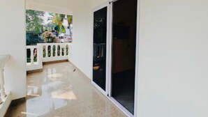 Um corredor com porta de vidro deslizante que dá para uma varanda com vista para áreas verdes e um edifício.