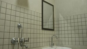 Casa de banho com lavatório branco, espelho e chuveiro.