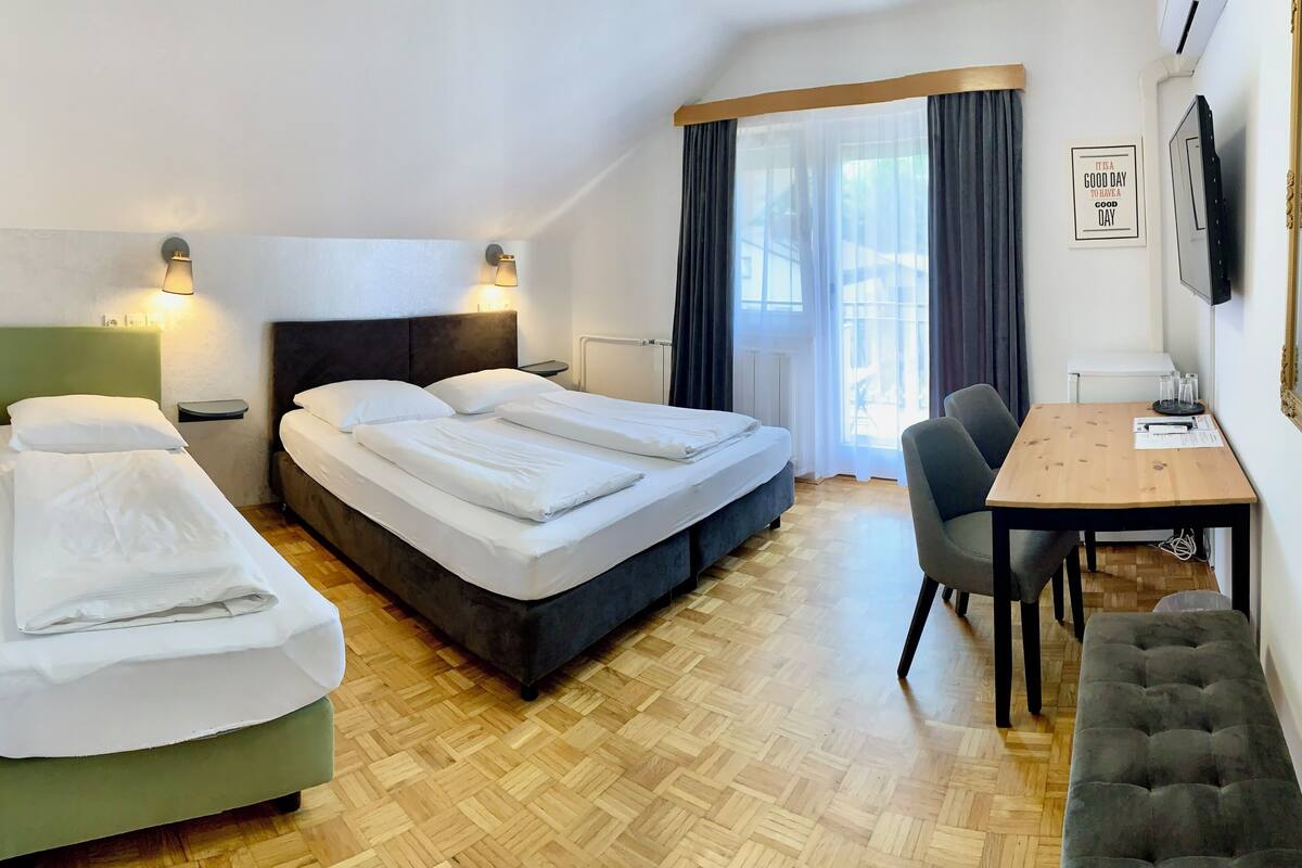Quarto de hotel com duas camas, uma escrivaninha, uma cadeira, uma televisão e uma janela com cortinas.