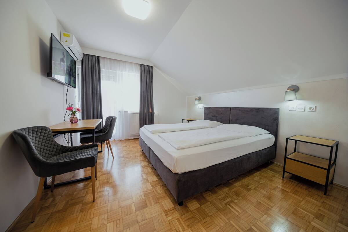 Quarto de hotel com cama, escrivaninha, cadeira, televisão e abajur.