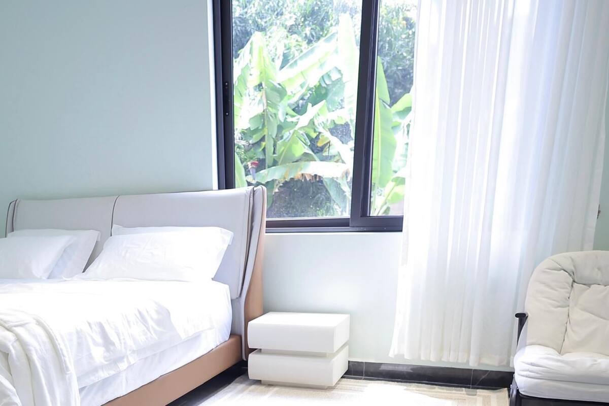 Quarto com cama, cadeira e janela com cortinas.