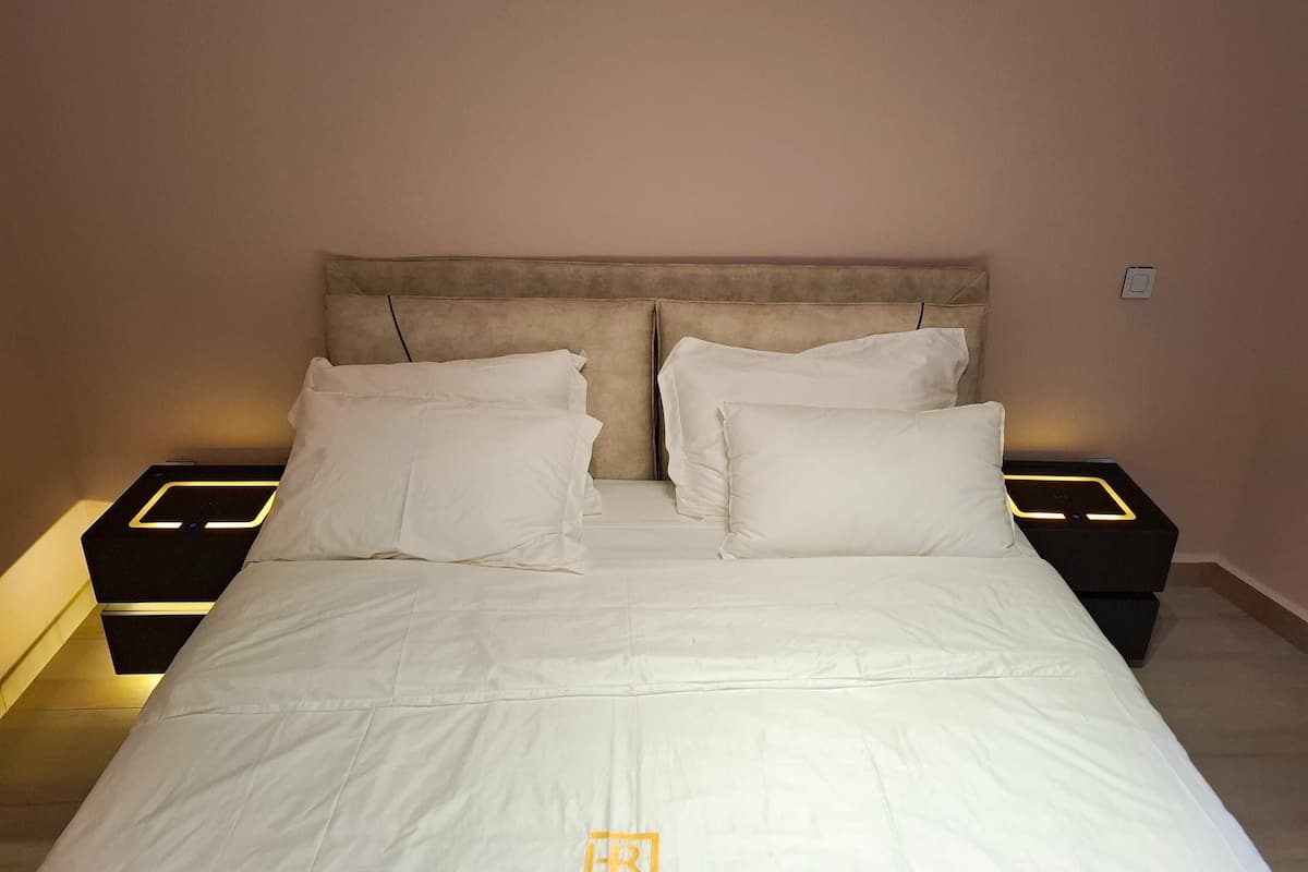 Cama bem arrumada com cabeceira, duas mesas de cabeceira e uma tomada na parede.