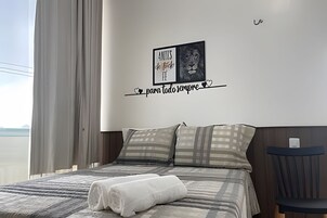 Quarto moderno com uma cama grande, vista para o mar e uma frase motivacional na parede.