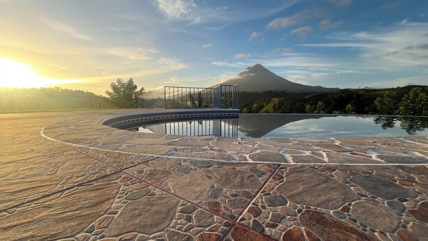 Uma piscina infinita com piso de pedra e uma passarela de vidro que leva a uma vista de montanhas.