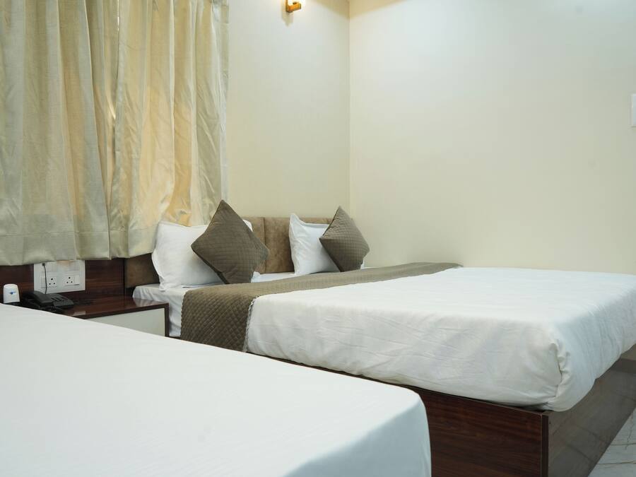 Quarto de hotel com duas camas, uma mesa de cabeceira com telefone, tomada e cortina.
