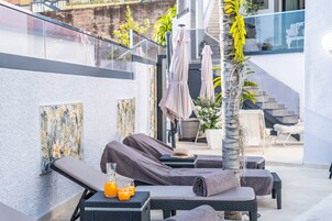 Uma área de estar ao ar livre moderna com cadeiras reclináveis, uma mesa com bebida e uma escadaria que leva a um andar superior.