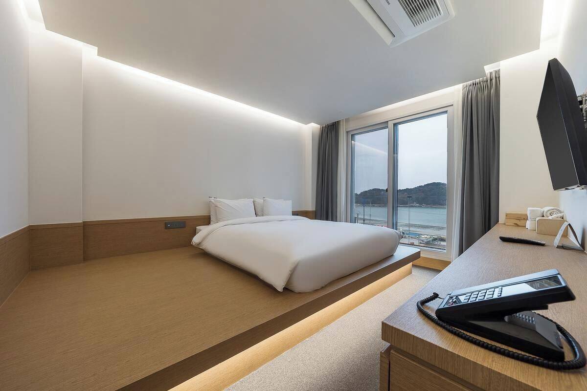 Quarto de hotel com cama, escrivaninha com telefone, janela com vista para o mar e televisão de tela plana.
