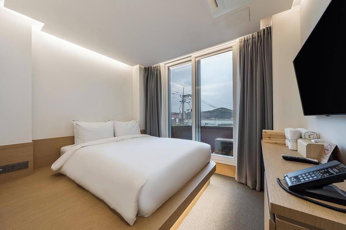 Quarto de hotel com uma cama grande, uma mesa com telefone e uma janela com cortinas.