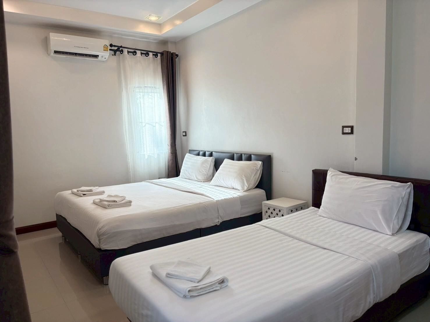 Quarto de hotel com duas camas, uma janela com cortinas, um aparelho de ar condicionado e uma mesa de cabeceira.