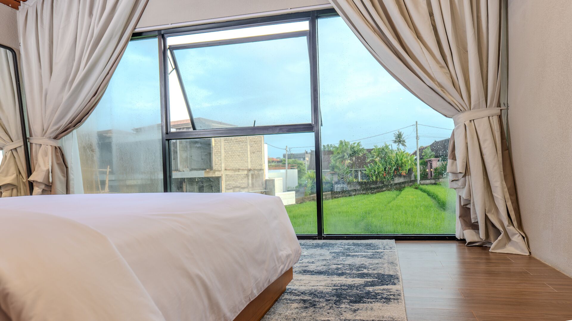 Quarto com uma janela ampla, uma cama e vista para uma paisagem verde.