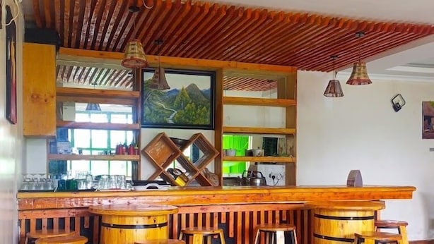 Uma área de bar com banquetas de madeira e balcão, com design rústico, teto de madeira e parede verde.