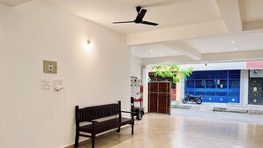 Quarto espaçoso com um banco de madeira, ventoinha no teto e vista para a rua.