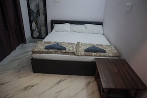 Cama com lençóis brancos e duas almofadas, um banco de madeira e piso de mármore.