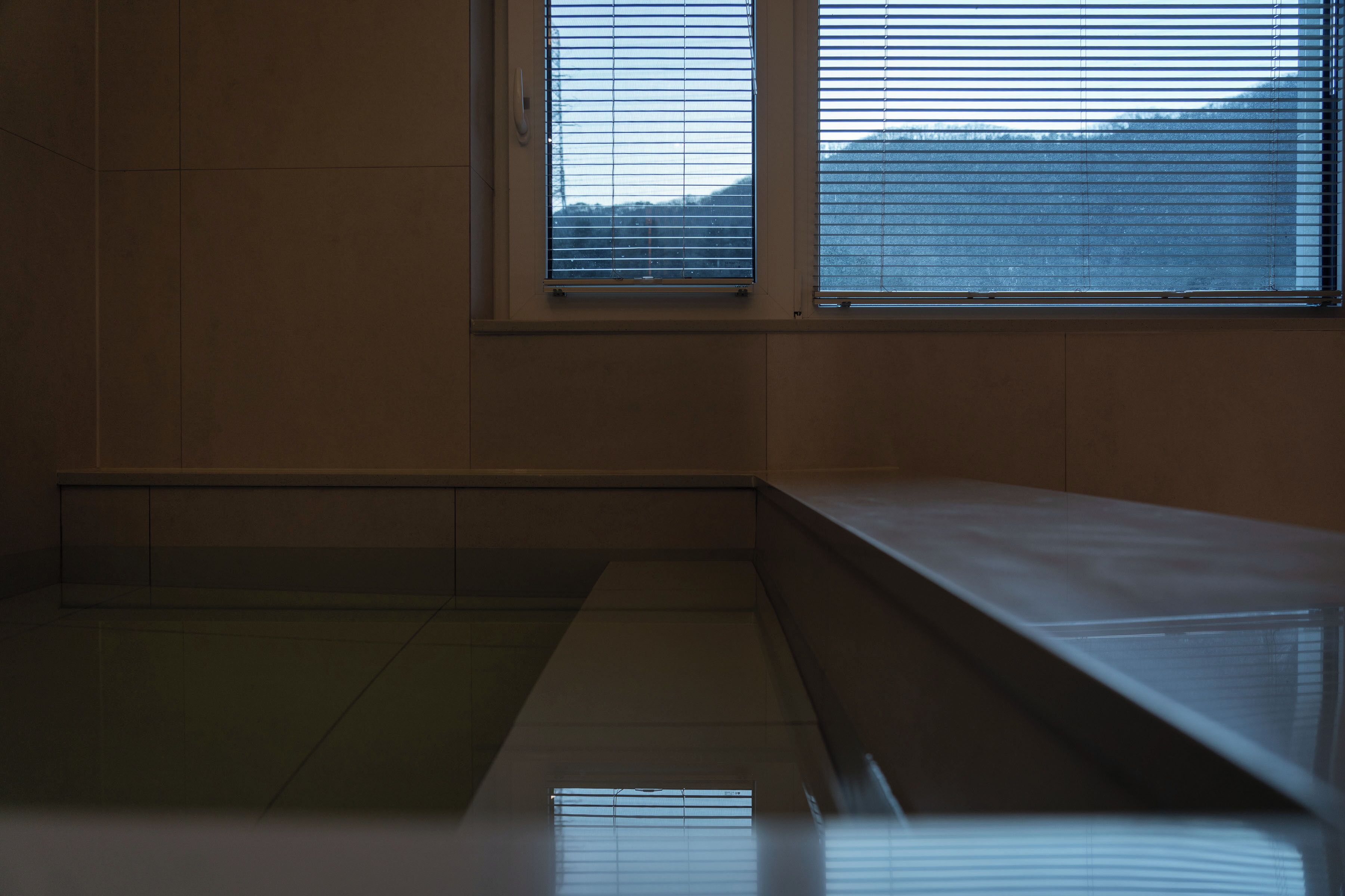 Um quarto com um banco, uma janela com persianas e um chão ladrilhado.