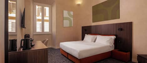 Quarto de hotel com cama, escrivaninha com cafeteira, cadeira e obras de arte nas paredes.